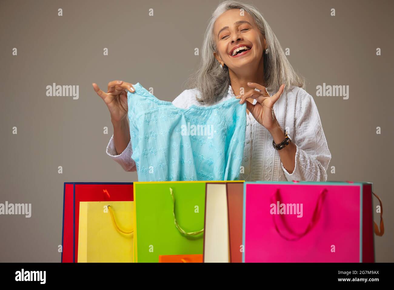 An old woman behind colorful handbags endearingly holding her new cloth ...