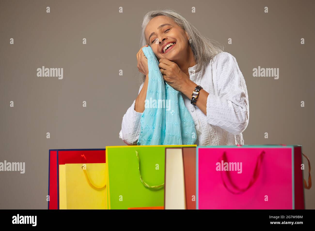 An old woman behind colorful handbags endearingly holding her new cloth ...