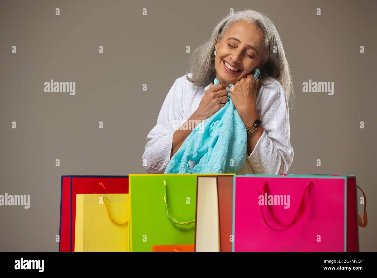 An old woman behind colorful handbags endearingly holding her new cloth ...