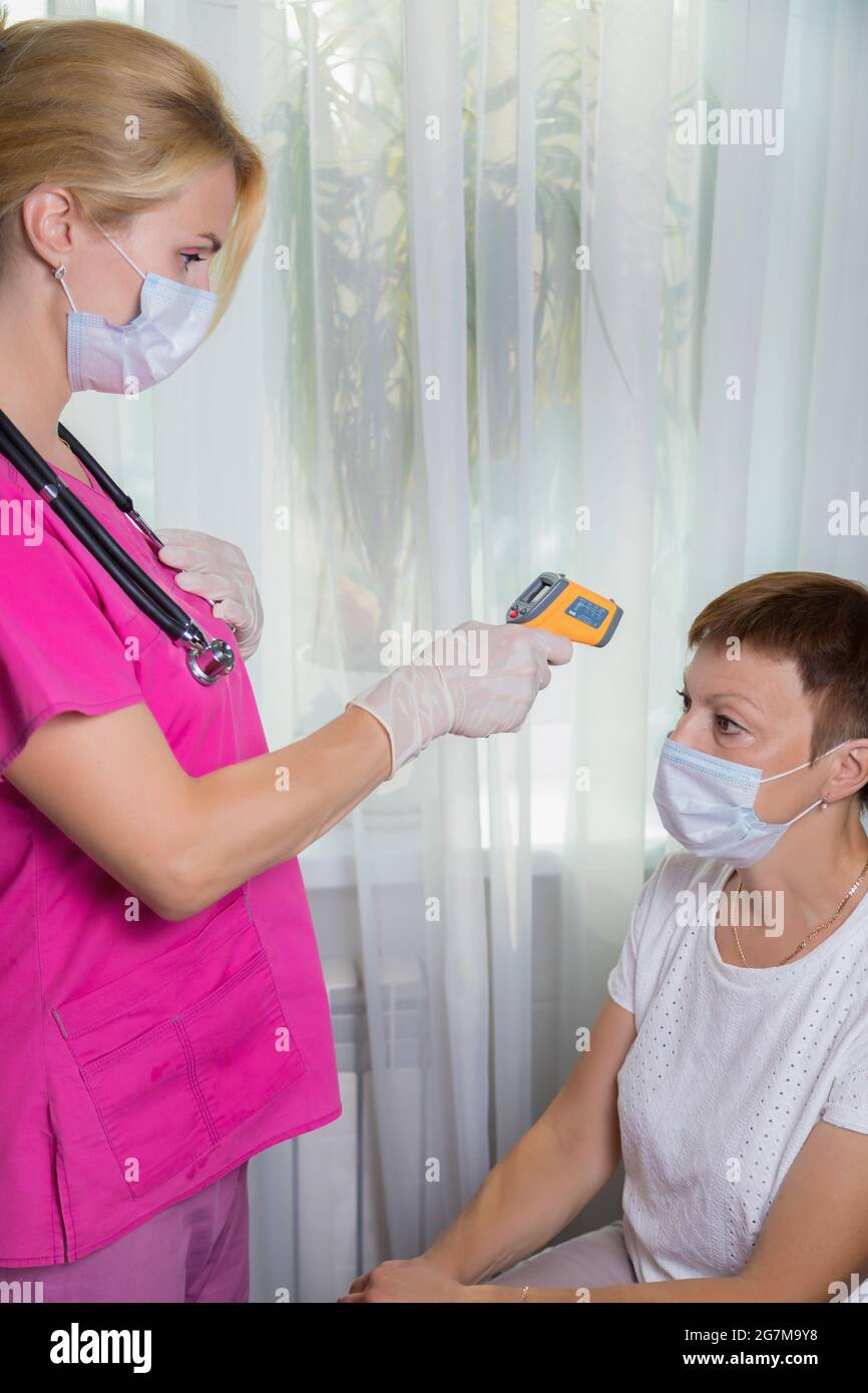 A female doctor measures the temperature of an adult woman with a laser ...