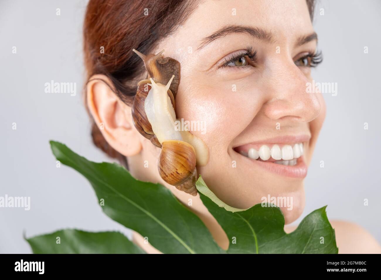 Beautiful caucasian smiling woman with snails on her face. Skin ...