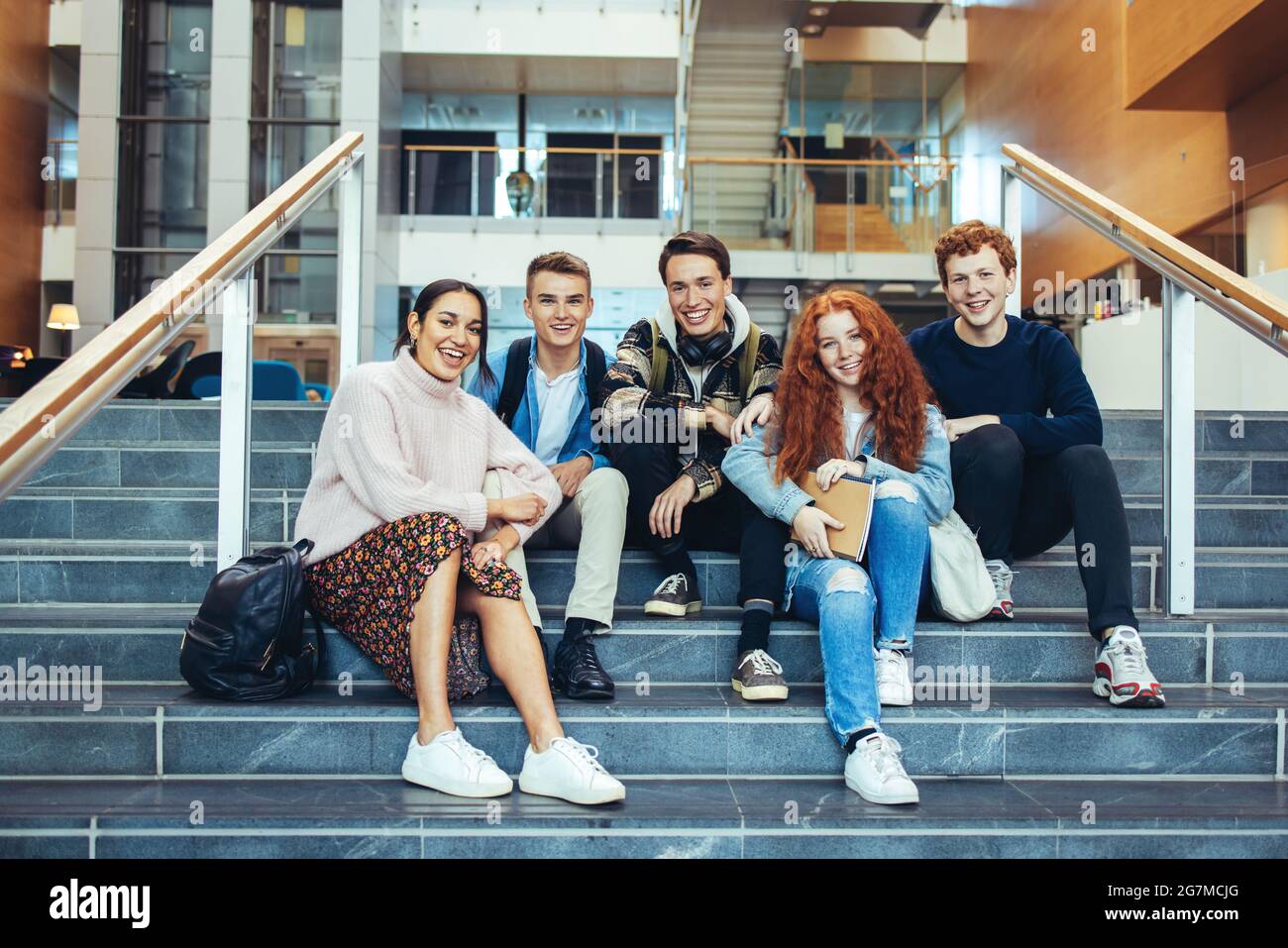 Young students smiling while sitting on college stairs. High school ...