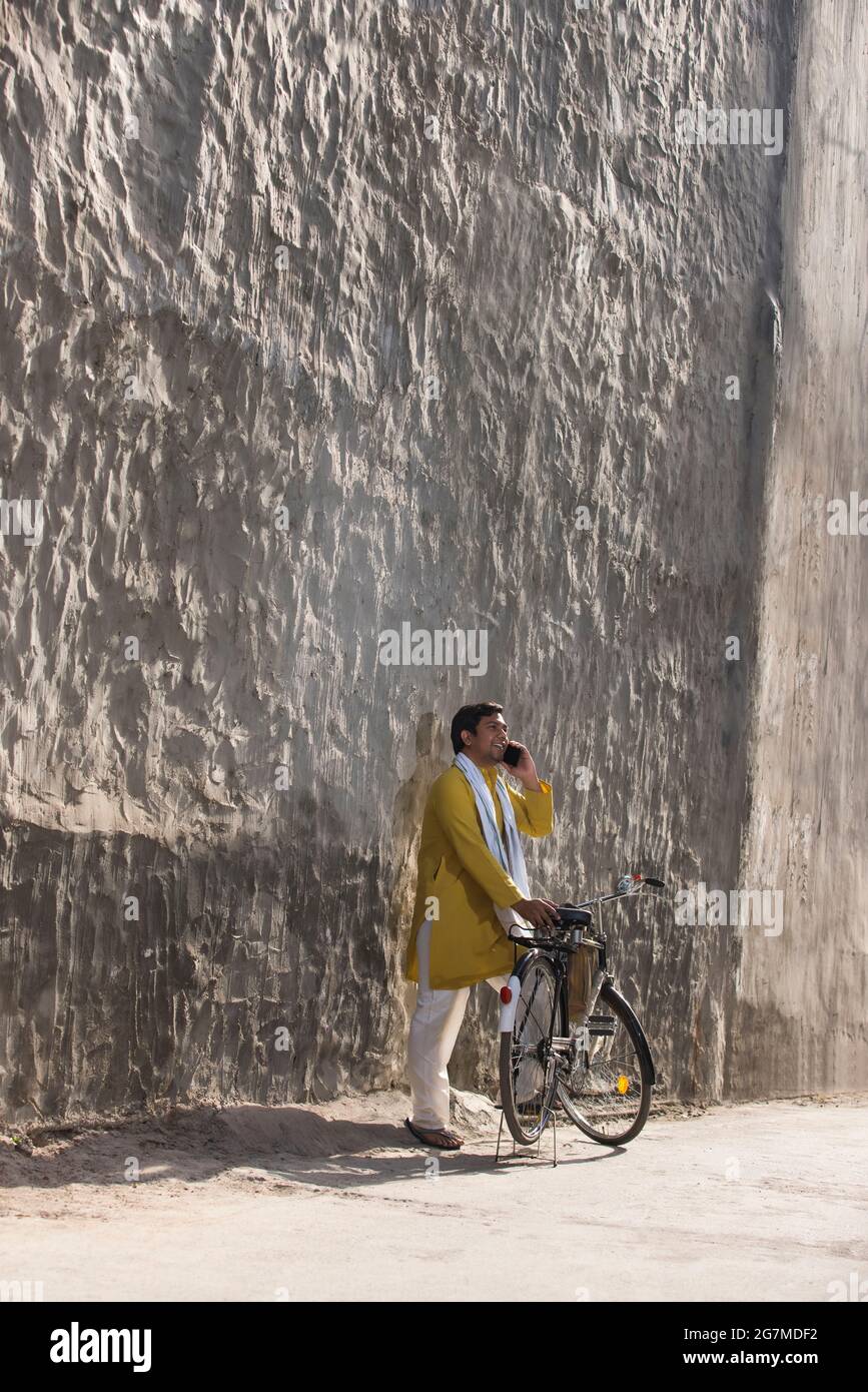 A VILLAGER STANDING AND TALKING ON MOBILE WHILE STANDING WITH CYCLE ...
