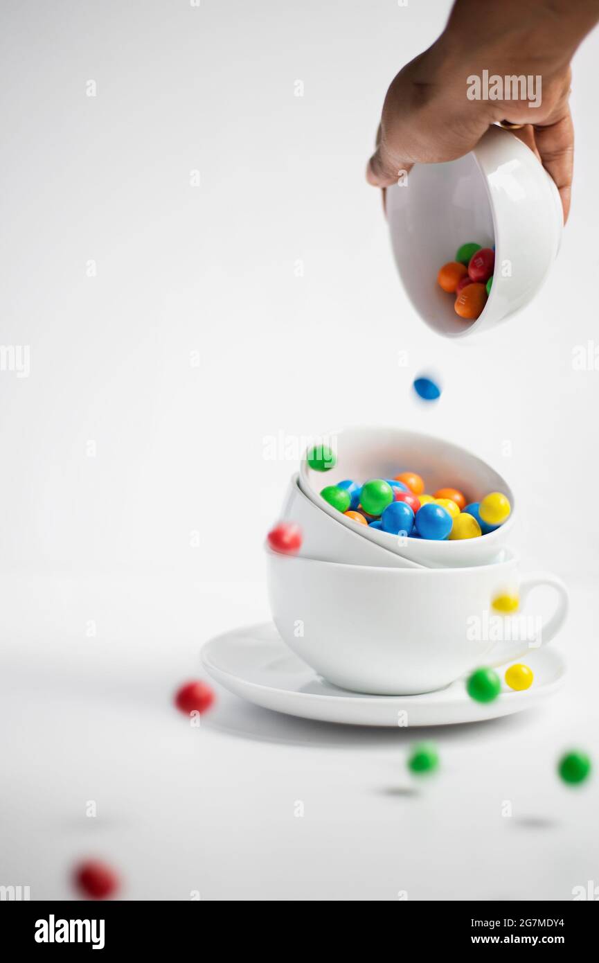 Vertical shot of hand pouring colorful candy balls on a cup isolated on ...