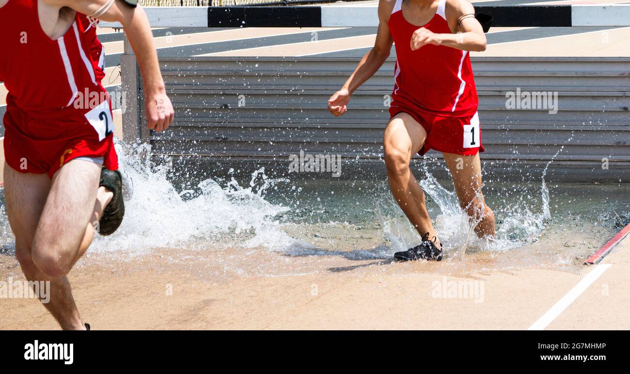 Two runners racing the steeplechase in red uniforms landing and running ...