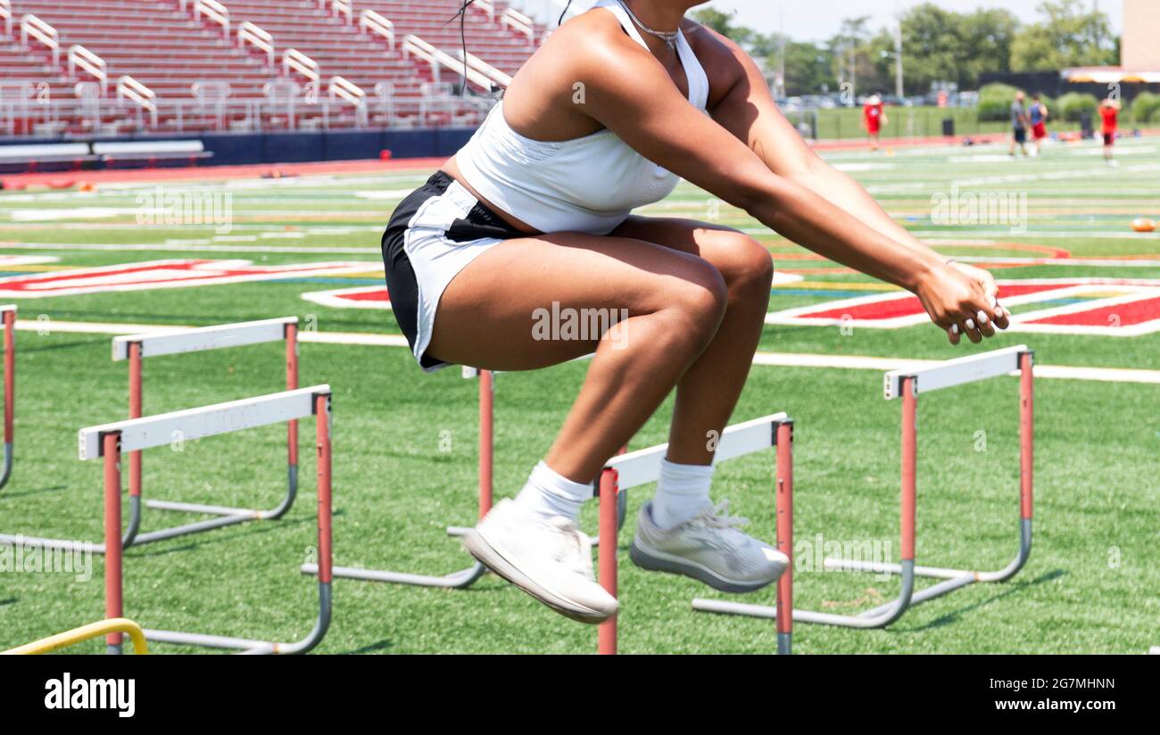 Side view of a young women working out jumping over track hurdles on a ...