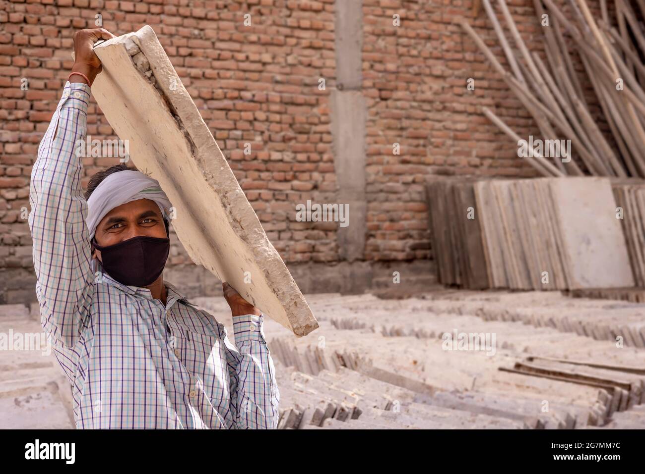 A MANUAL LABOURER WEARING FACE MASK LIFTING LARGE BLOCK OF TILE Stock ...