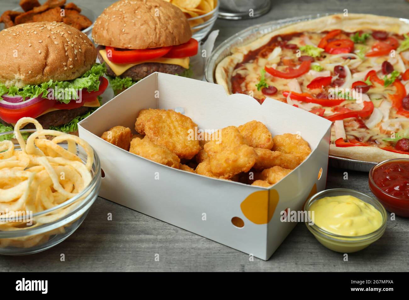 Different fast food on gray textured table Stock Photo - Alamy