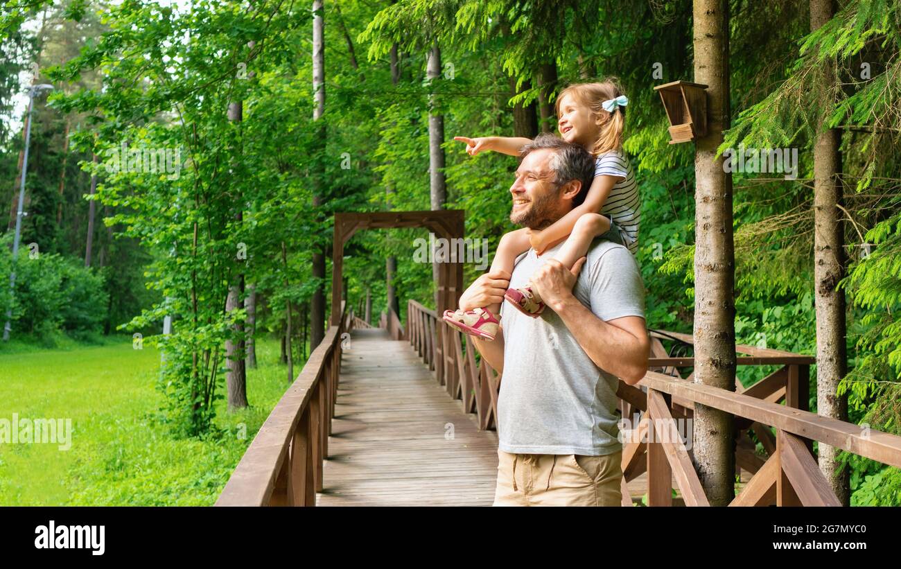 The father carries his daughter on his shoulders while walking along the hiking trail in the ...
