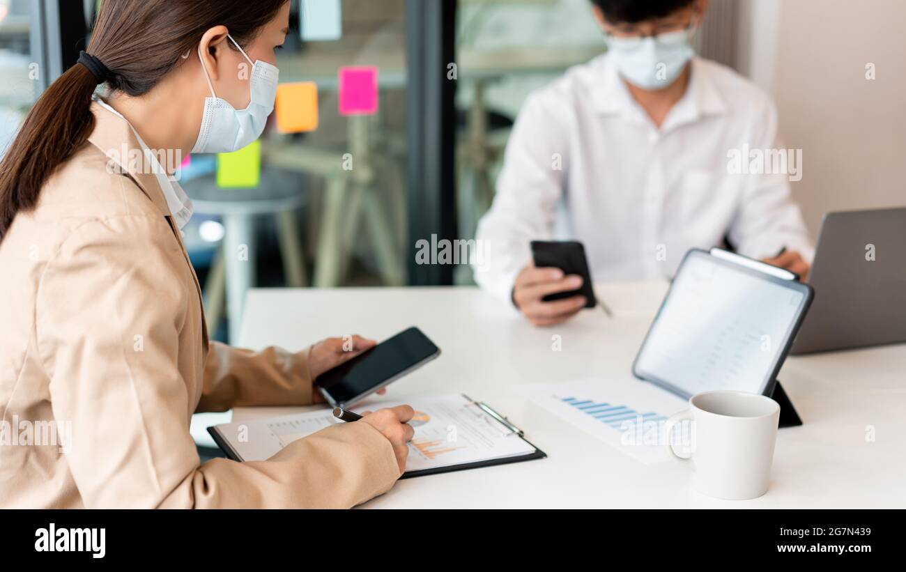 Two colleagues wearing surgical masks analyzing the data in chart for ...