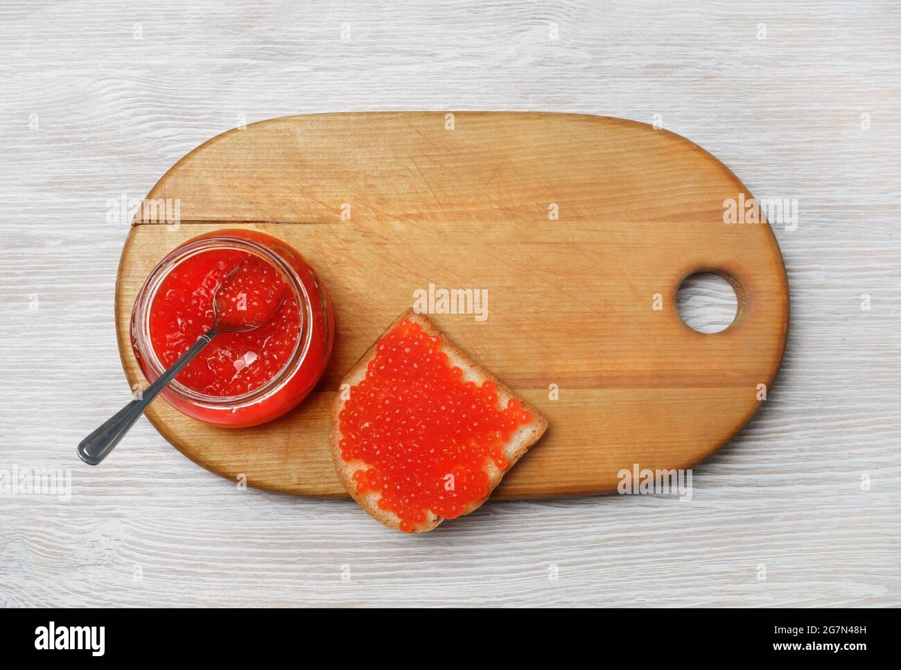 Sandwich with red caviar, glass jar and spoon on wooden cutting board ...