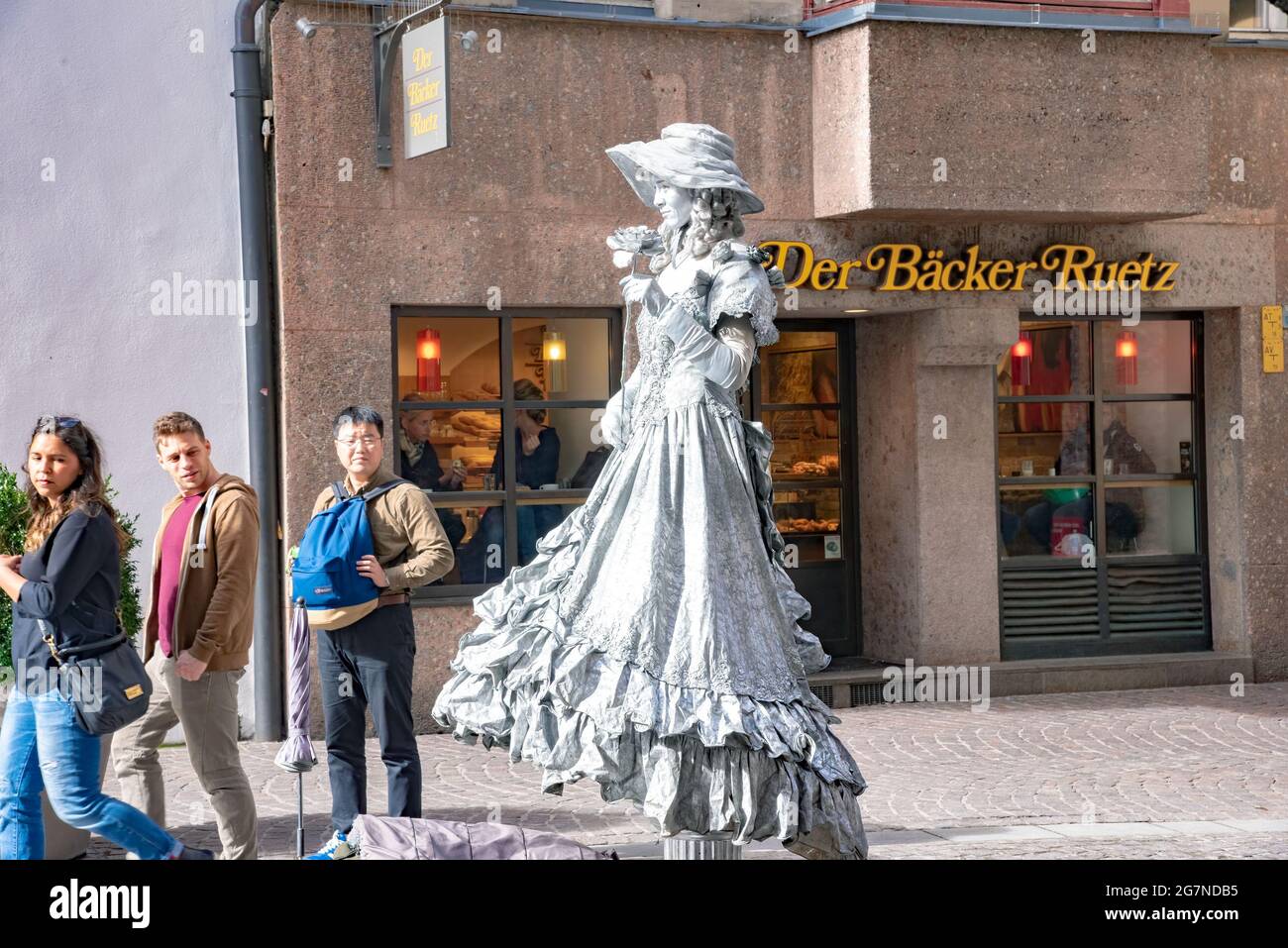 A street performer dressed in silver metallic gown posing as a living ...
