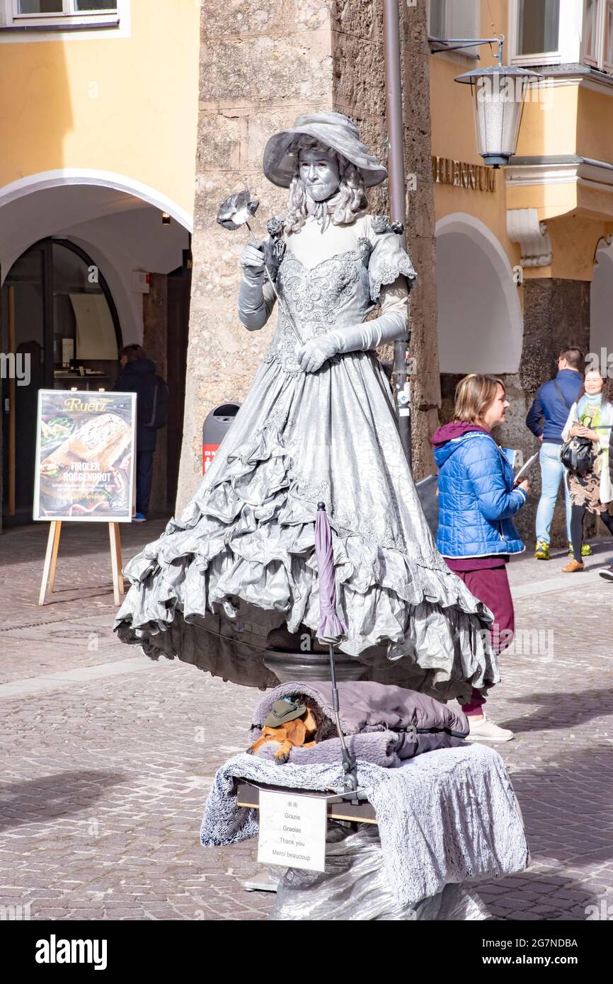 A street performer dressed in silver metallic gown posing as a living ...