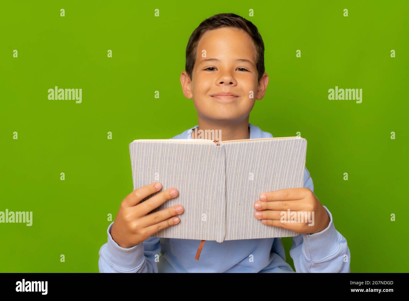 Happy schoolboy sitting on the desk reading a book isolated over green ...