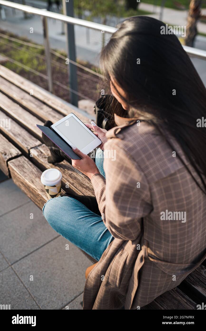Long-haired brunette woman reading an electronic book with blank screen ...