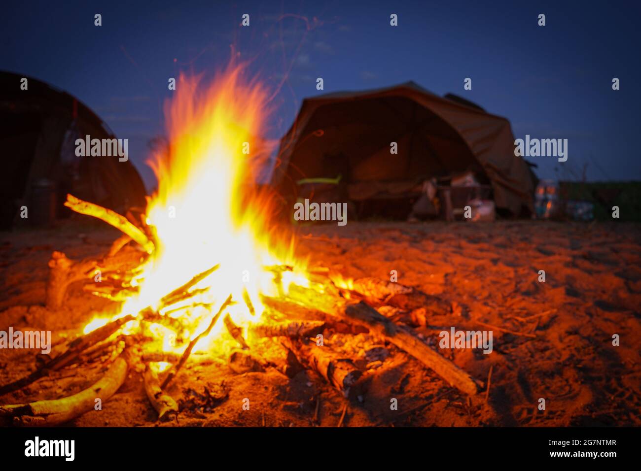 Closeup of a campfire with tents in a camping area at night in the ...
