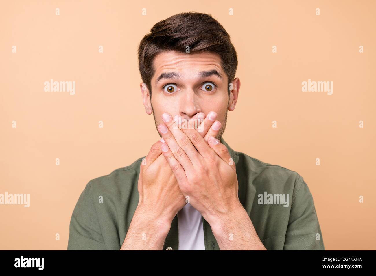 Photo of afraid scared young man hold hands cover mouth face tell ...
