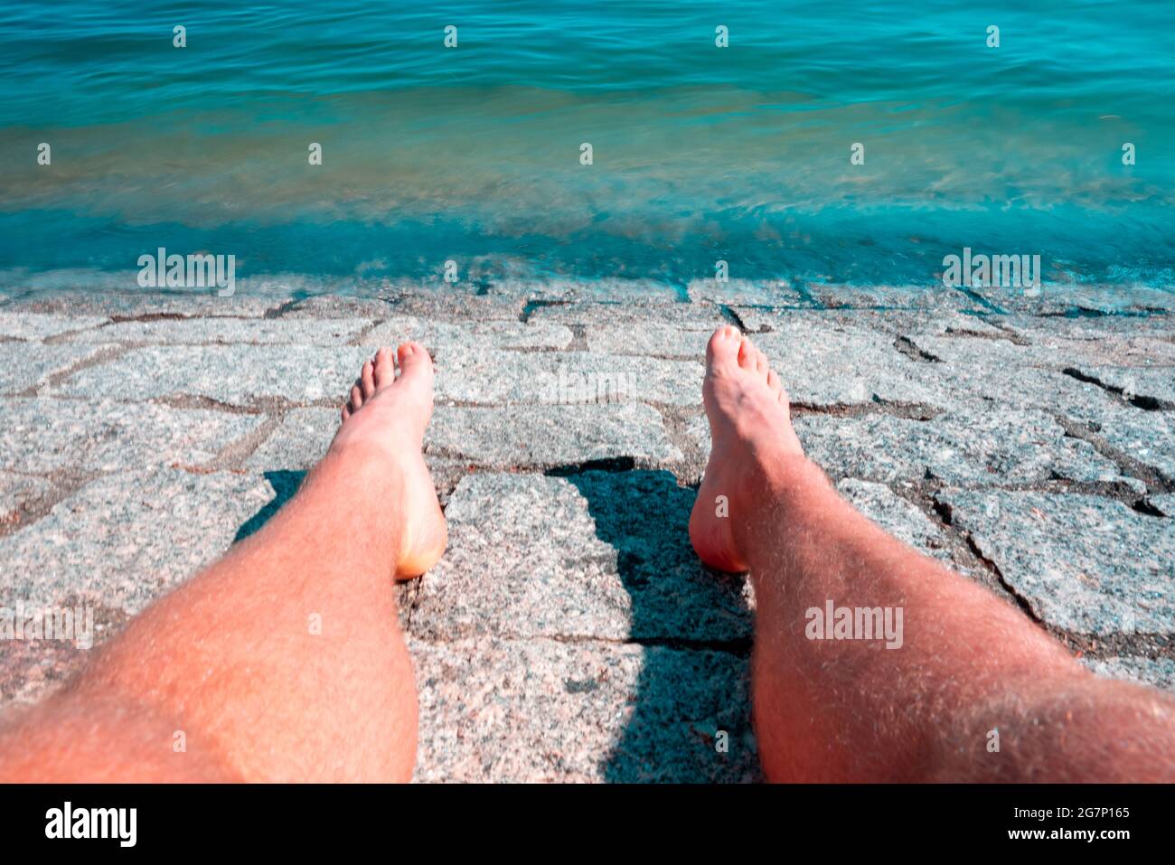 Beautiful clear blue ocean in front of Caucasian male legs tanning ...