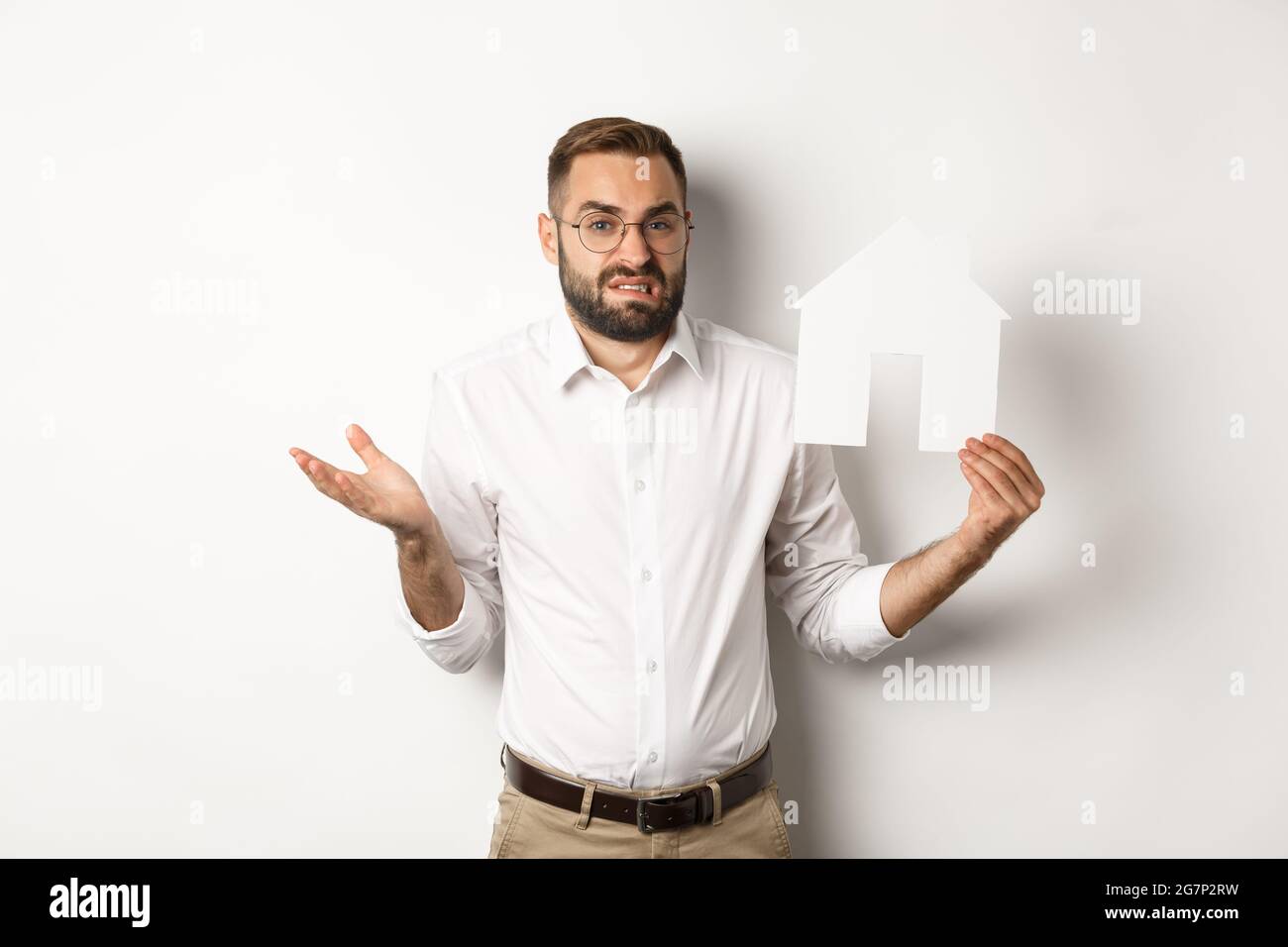 Real estate. Confused man shrugging, showing house paper model and ...
