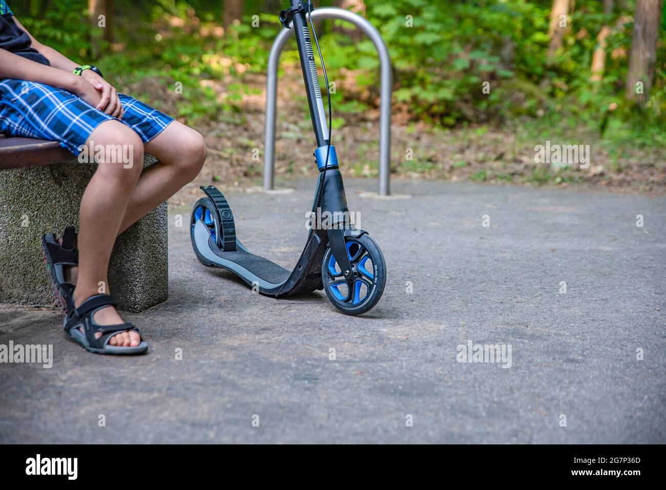 Walk in the park on a scooter. A young guy sits on a bench and rests ...