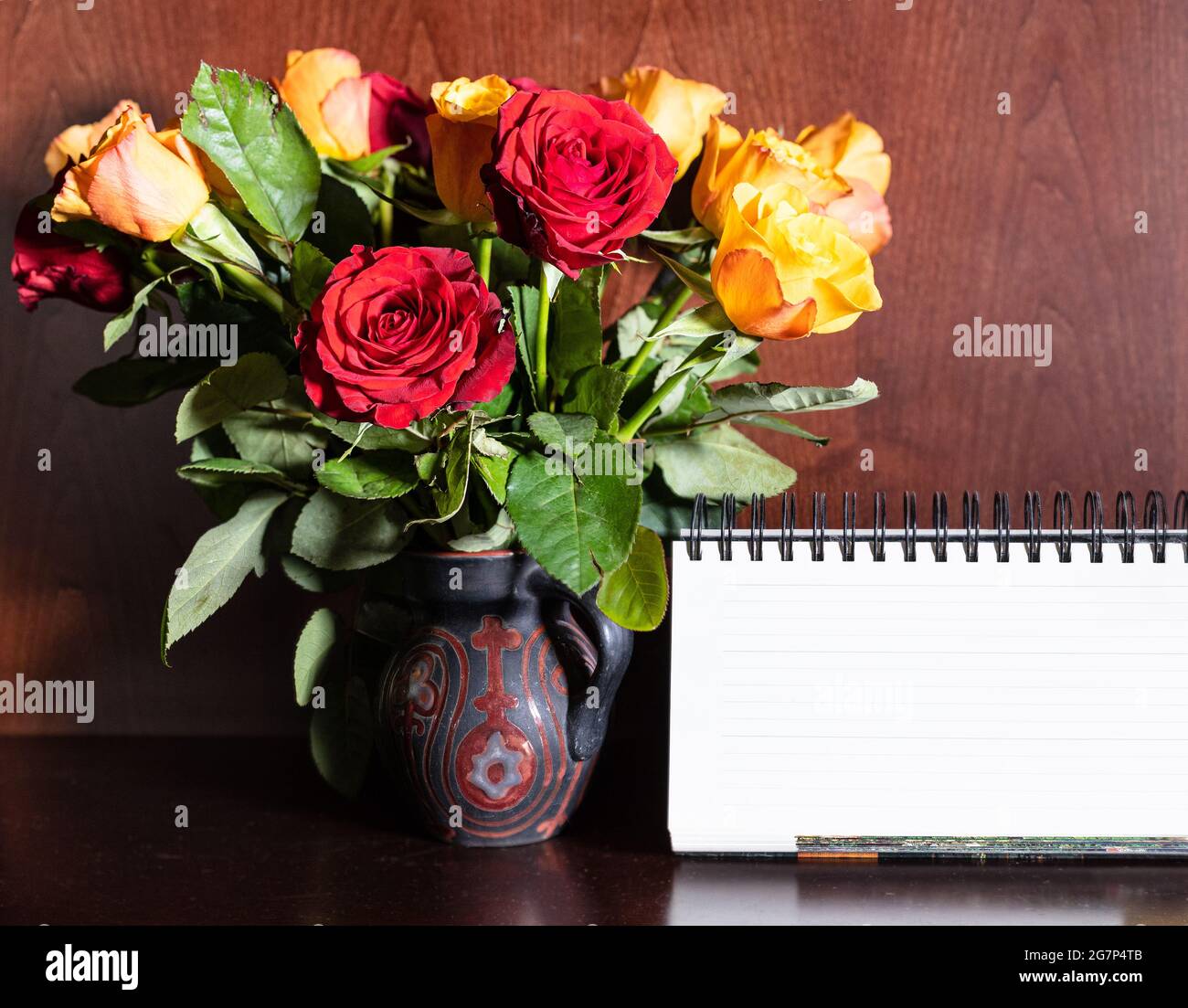blank desk calendar and fresh red and yellow roses in ceramic jug on ...