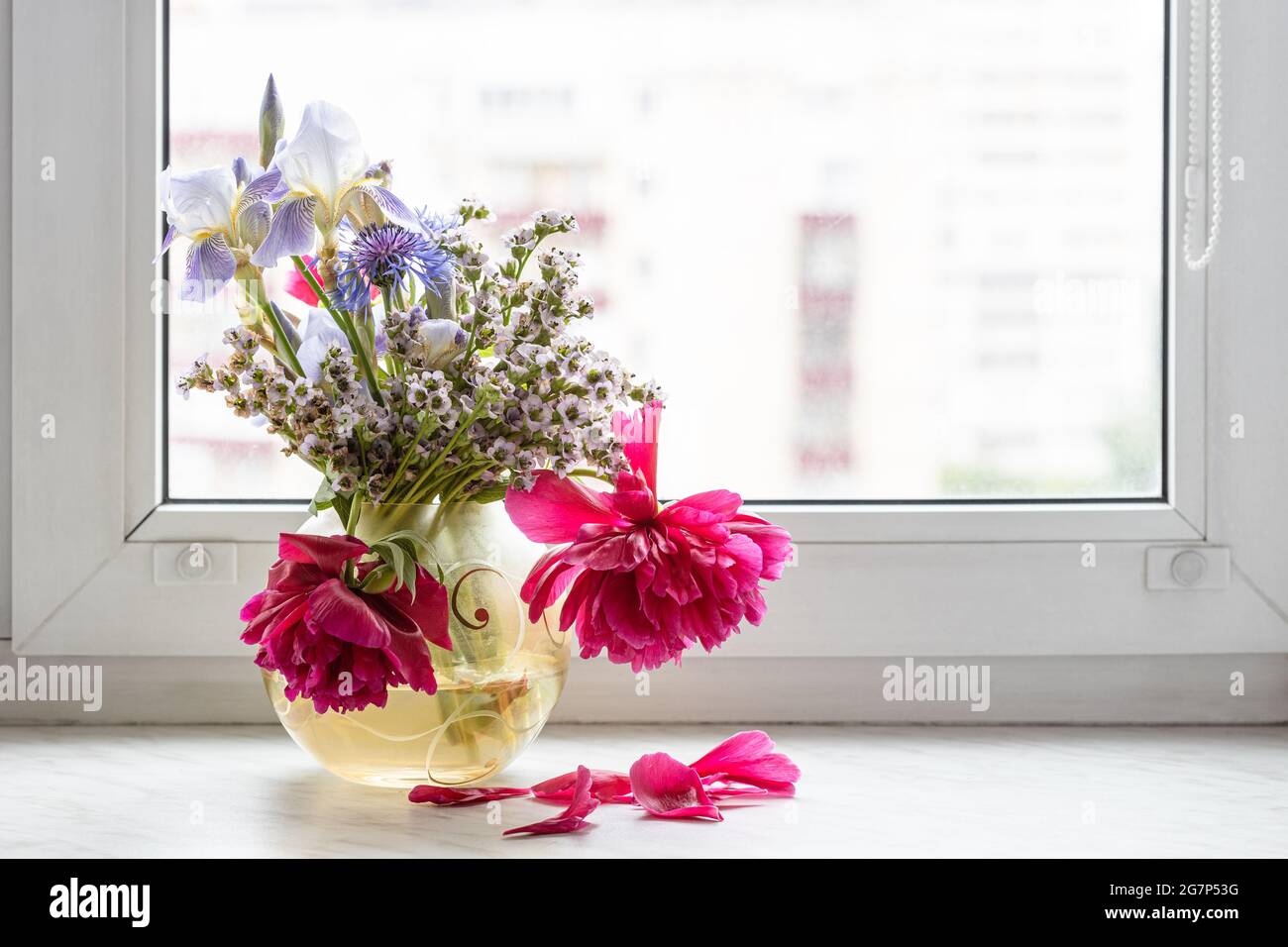 withered flowers in glass vase on window sill at home with cityscape on ...