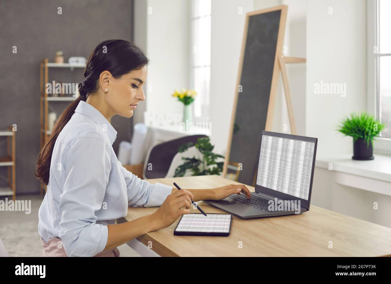 Woman sitting at office desk, working on laptop and tablet computers ...