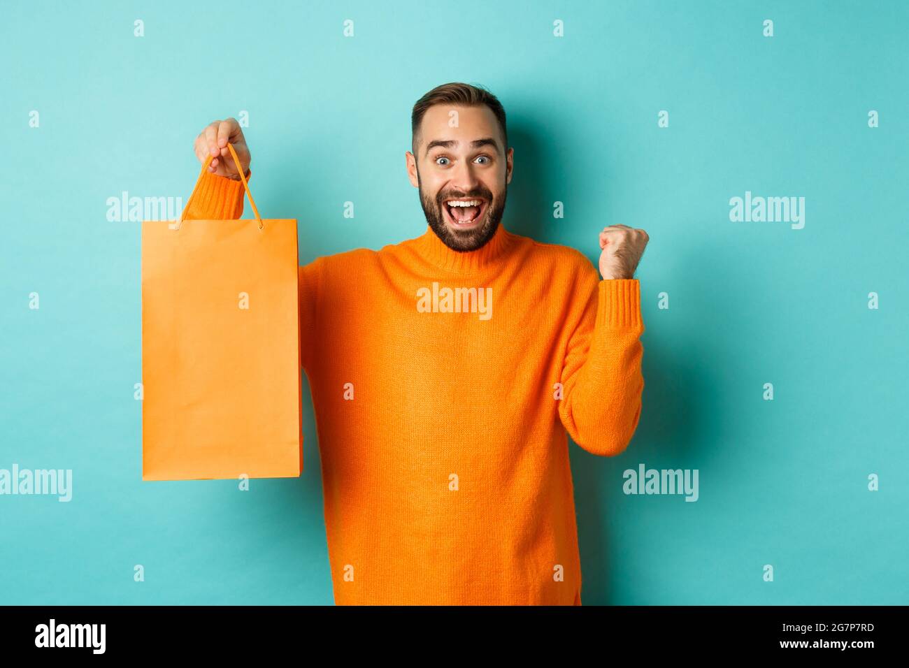 Happy man holding orange shopping bag and rejoicing, got discount and ...