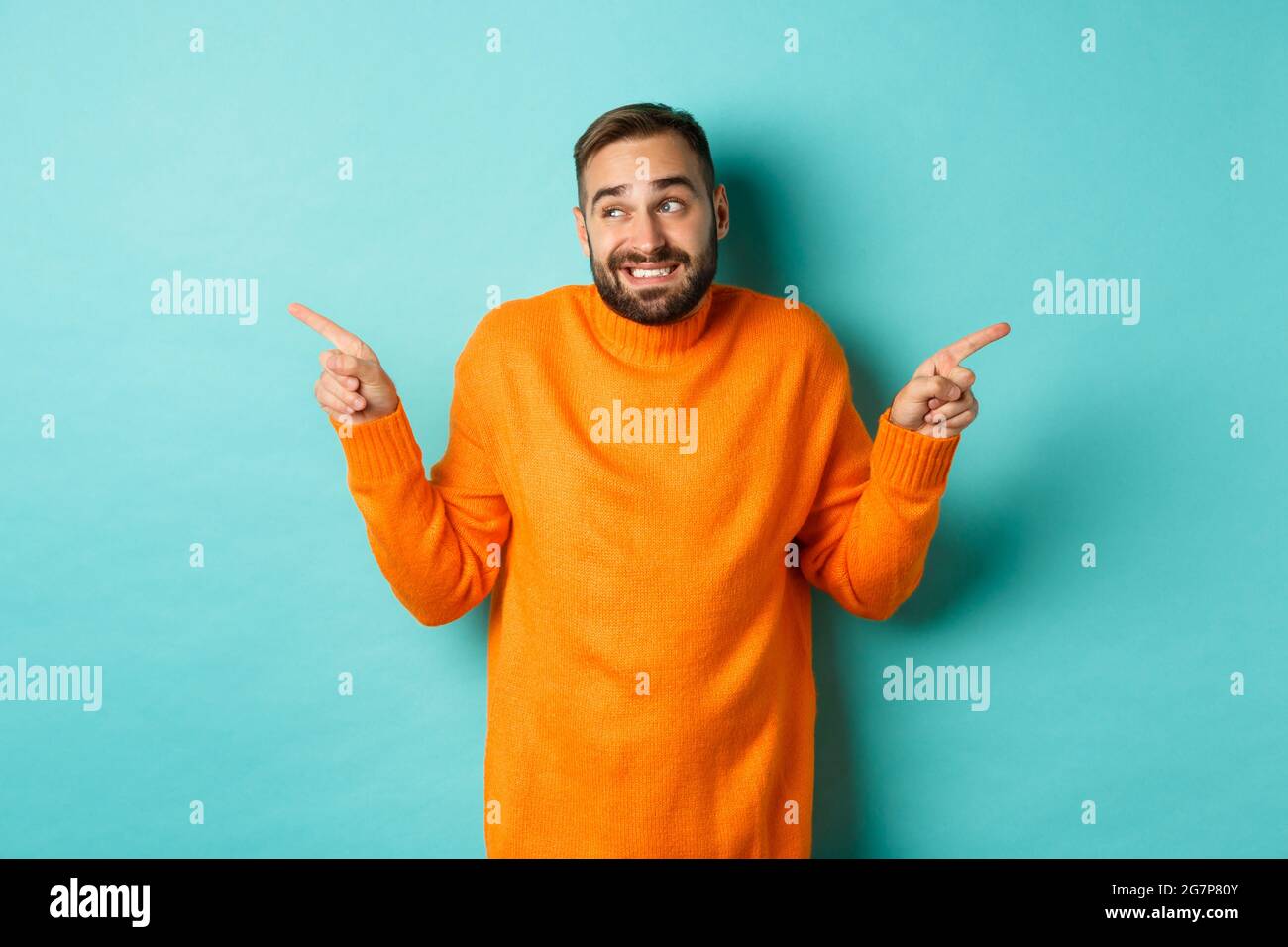 Confused handsome man shrugging indecisive, pointing fingers sideways ...