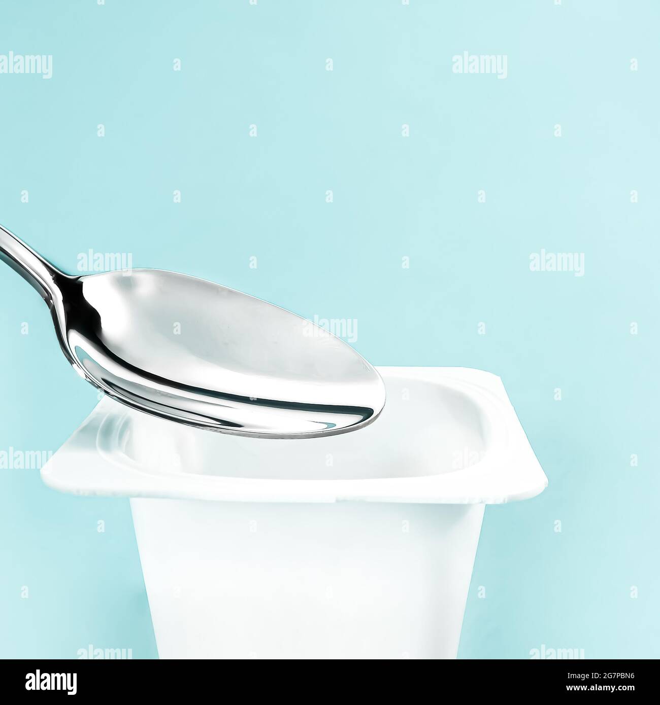 Yogurt cup and silver spoon on mint background, white plastic container ...