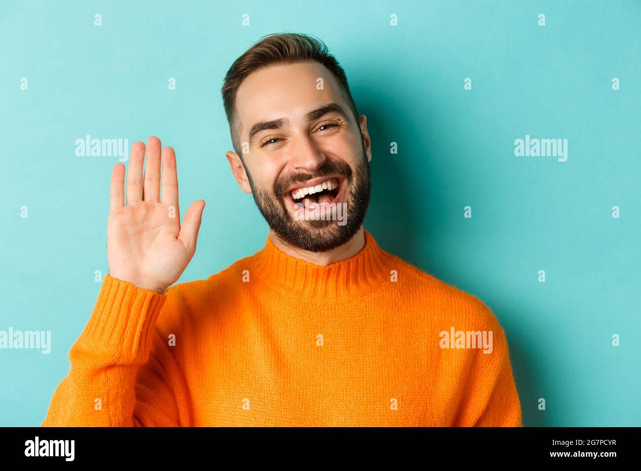 Close-up of friendly young man smiling, waving hand to say hello ...