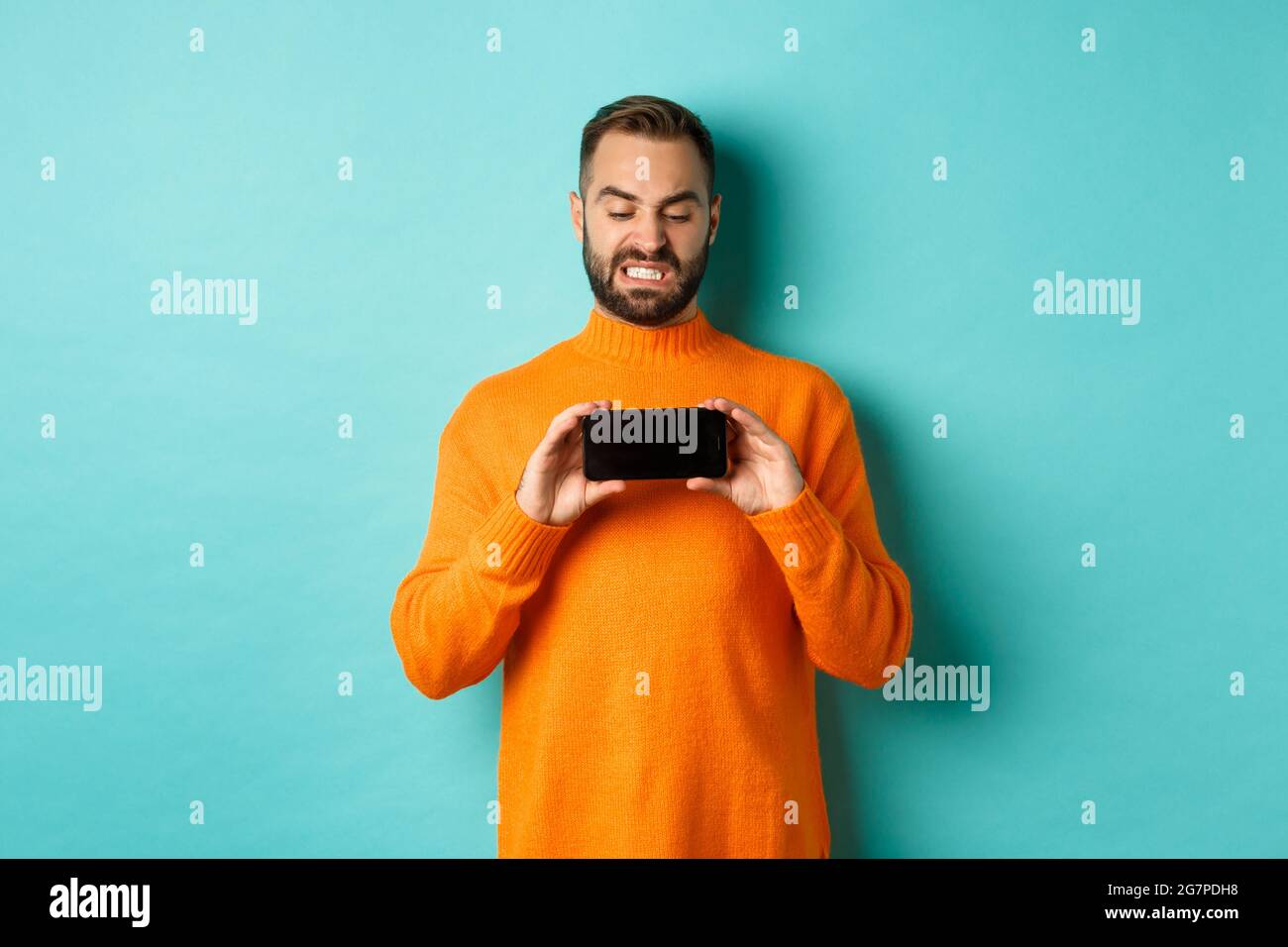 Image of man cringe at something on mobile screen, staring disgusted at ...