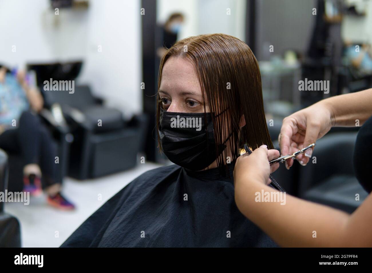 Caucasian lady getting her hair cut in a salon wearing a sanitary mask ...
