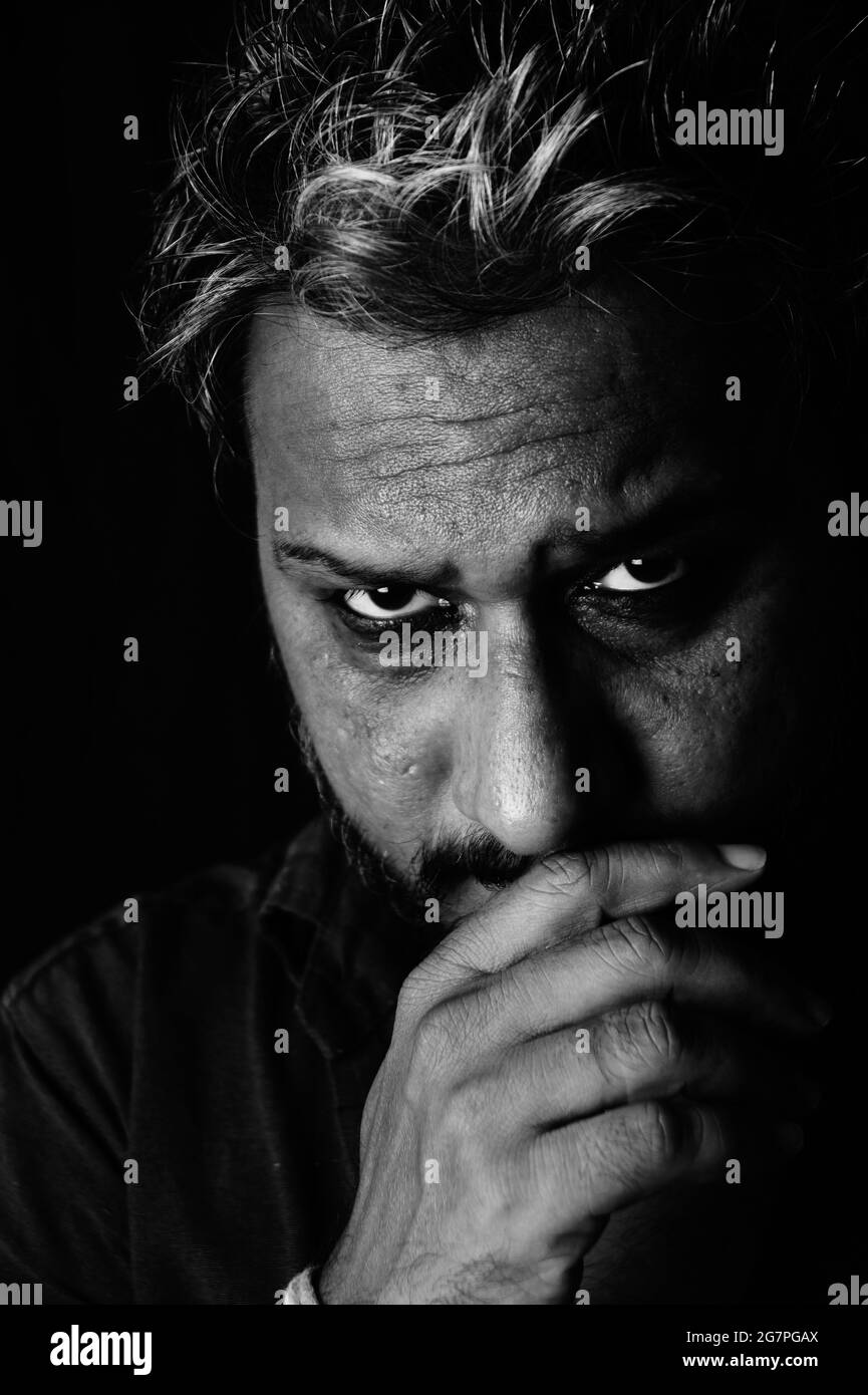 Grayscale portrait of a man with angry eyes and a beard with his hand ...