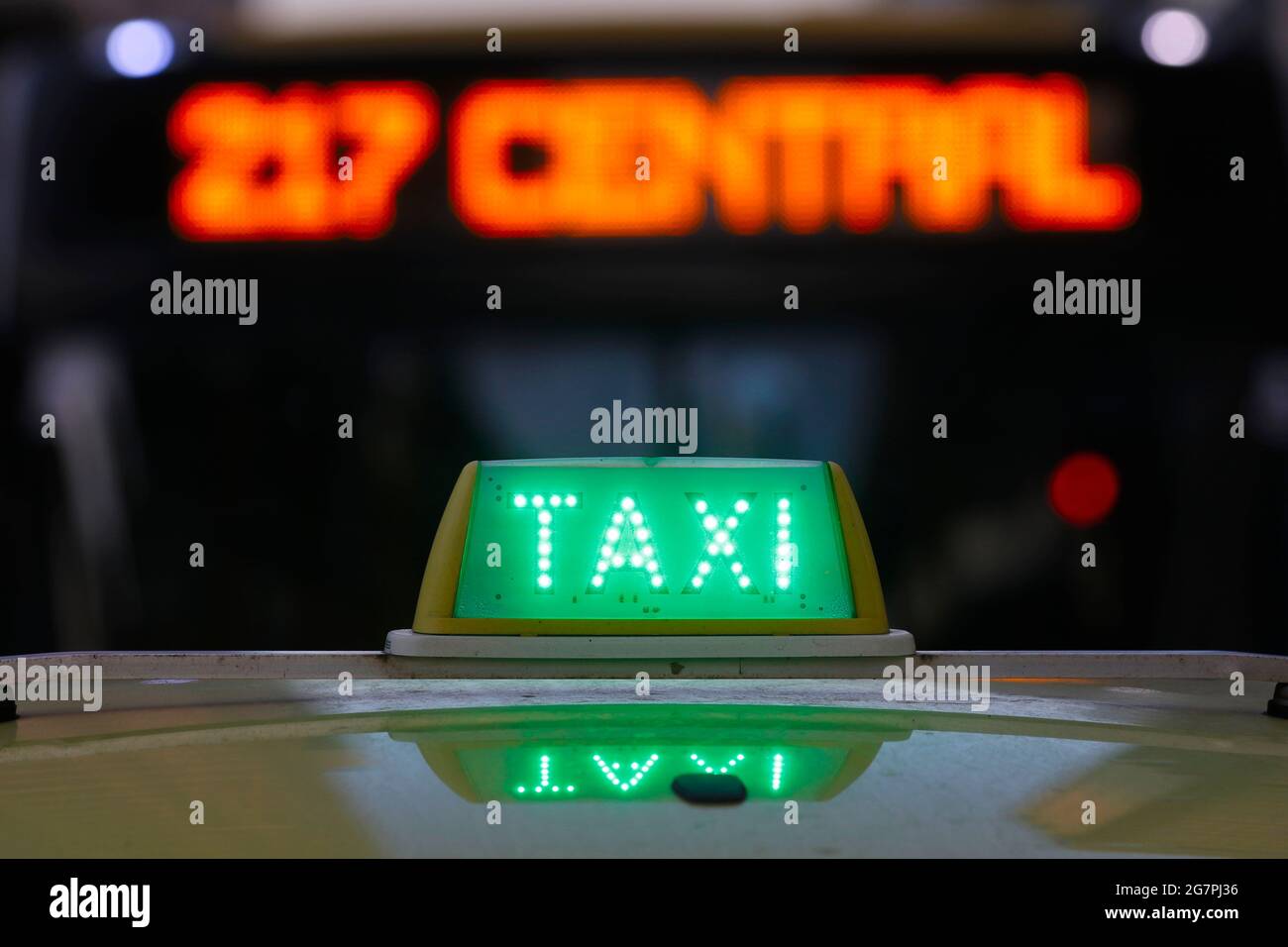 Taxi cab sign illuminated on top of vehicle at nighttime. City traffic ...