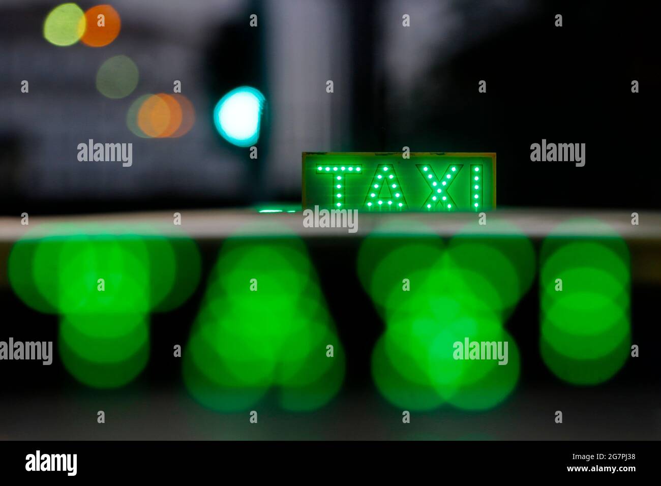 Taxi cab sign illuminated on top of vehicle at nighttime. City traffic ...