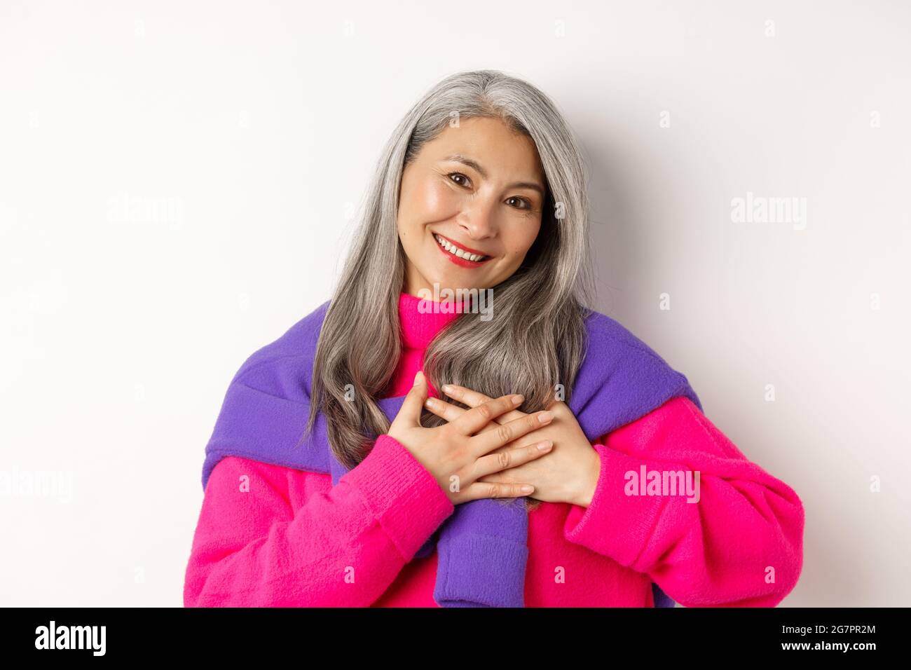 Close up of stylish asian mother holding hands on heart, looking ...