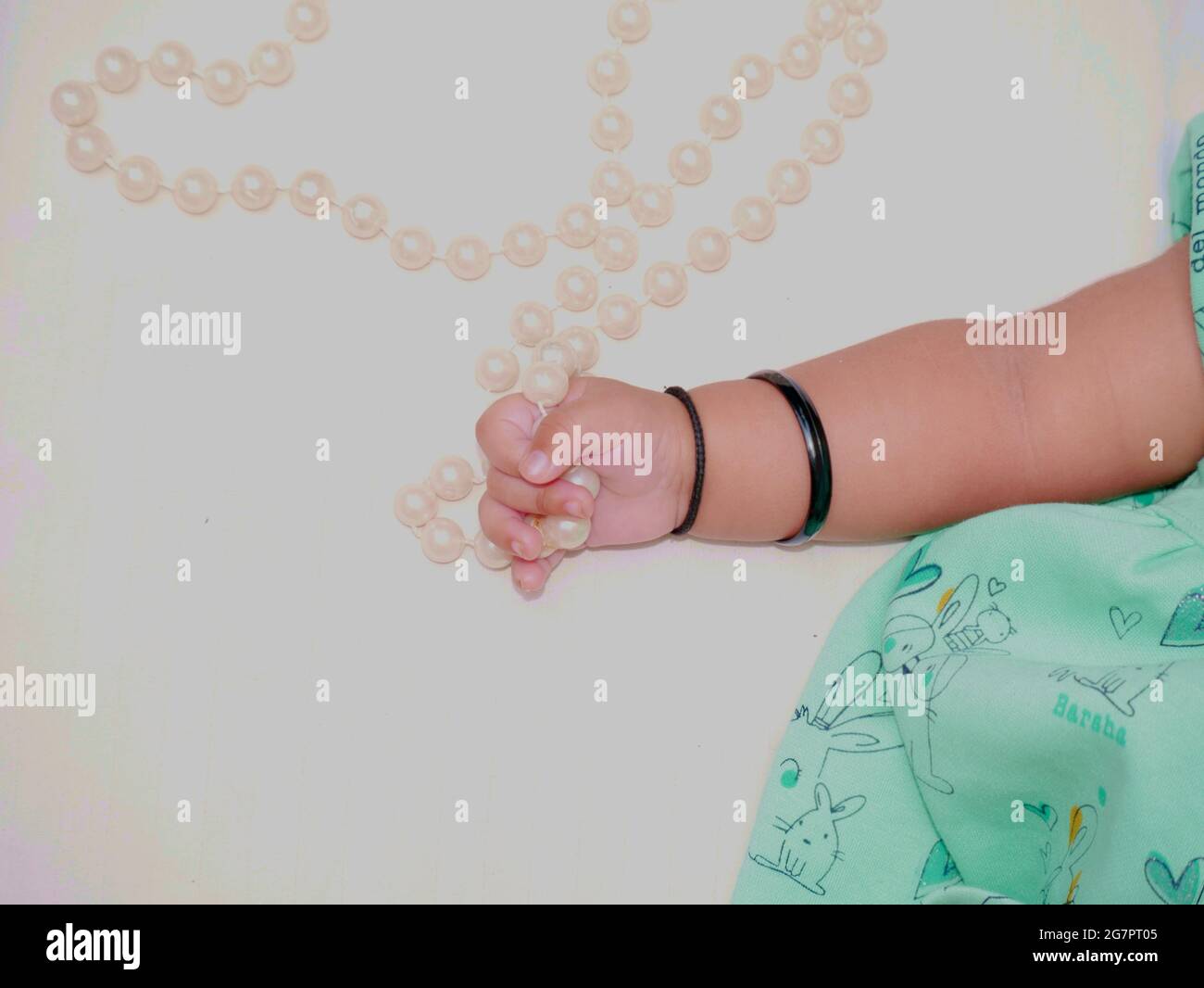 new born baby girl hand holding pearls garland gold color on white ...