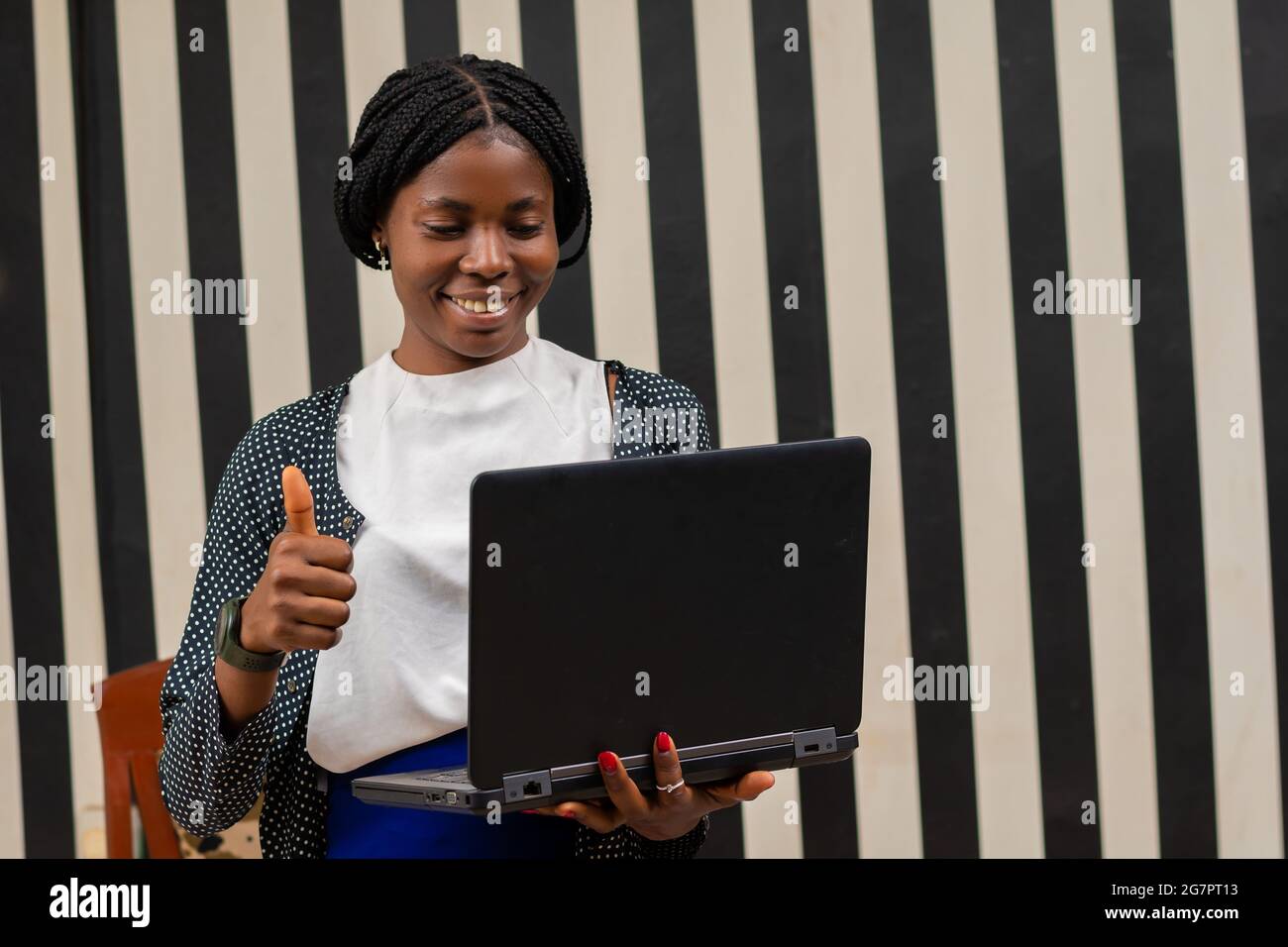 Happy Nigerian woman in her workplace holding her laptop and raising ...