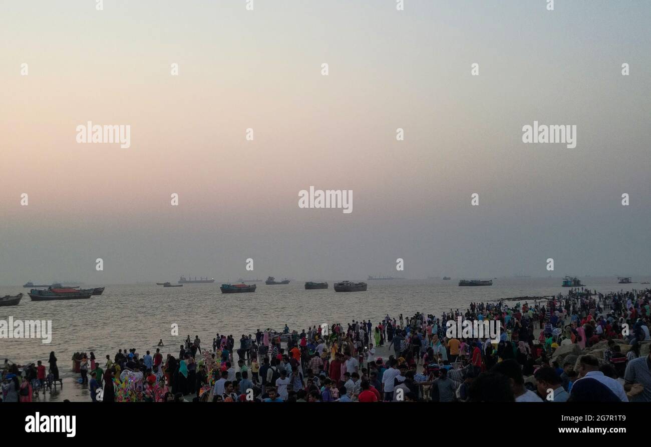 Large crowd gathered at the shore on a beach under a gradient sky ...