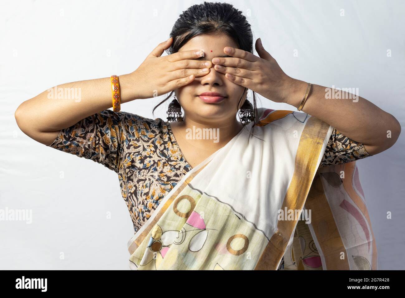 Isolated on white background an Indian woman in saree covering her eyes ...