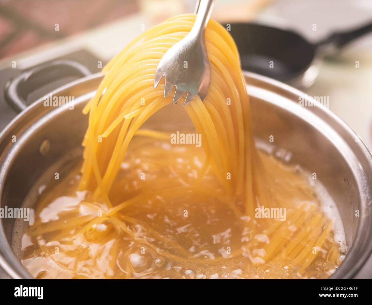 Raw spaghetti is being cooked in boiling water in a kitchen pot ...
