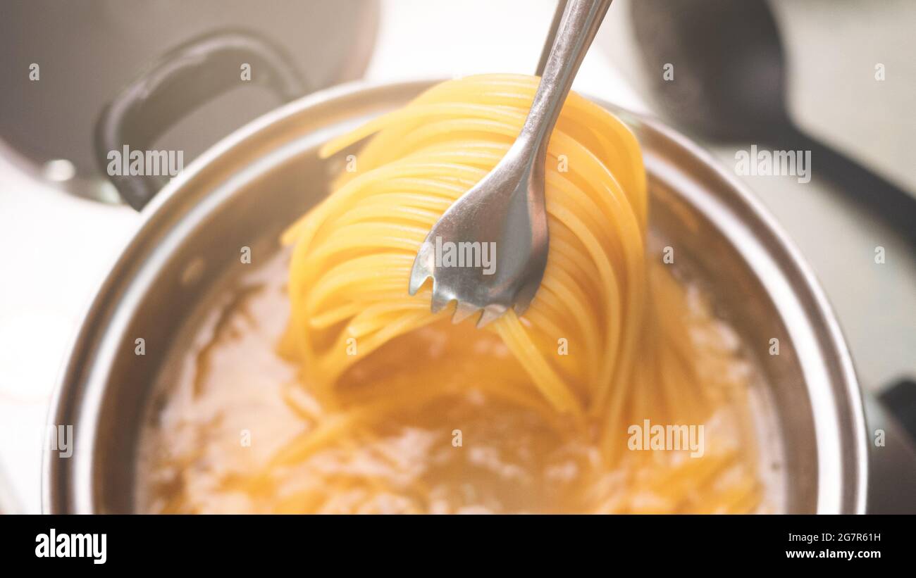 Raw spaghetti is being cooked in boiling water in a kitchen pot ...