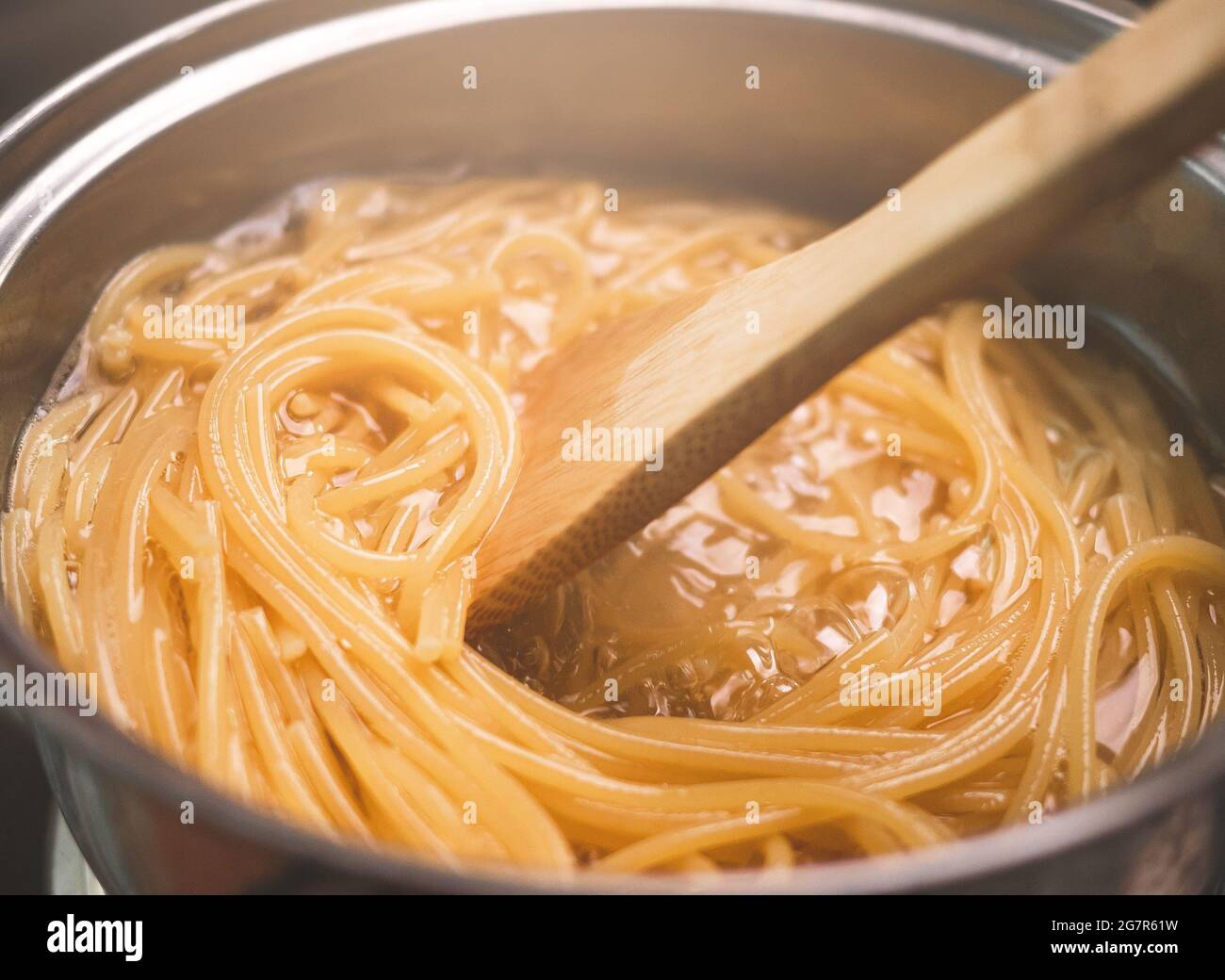 Raw spaghetti is being cooked in boiling water in a kitchen pot ...