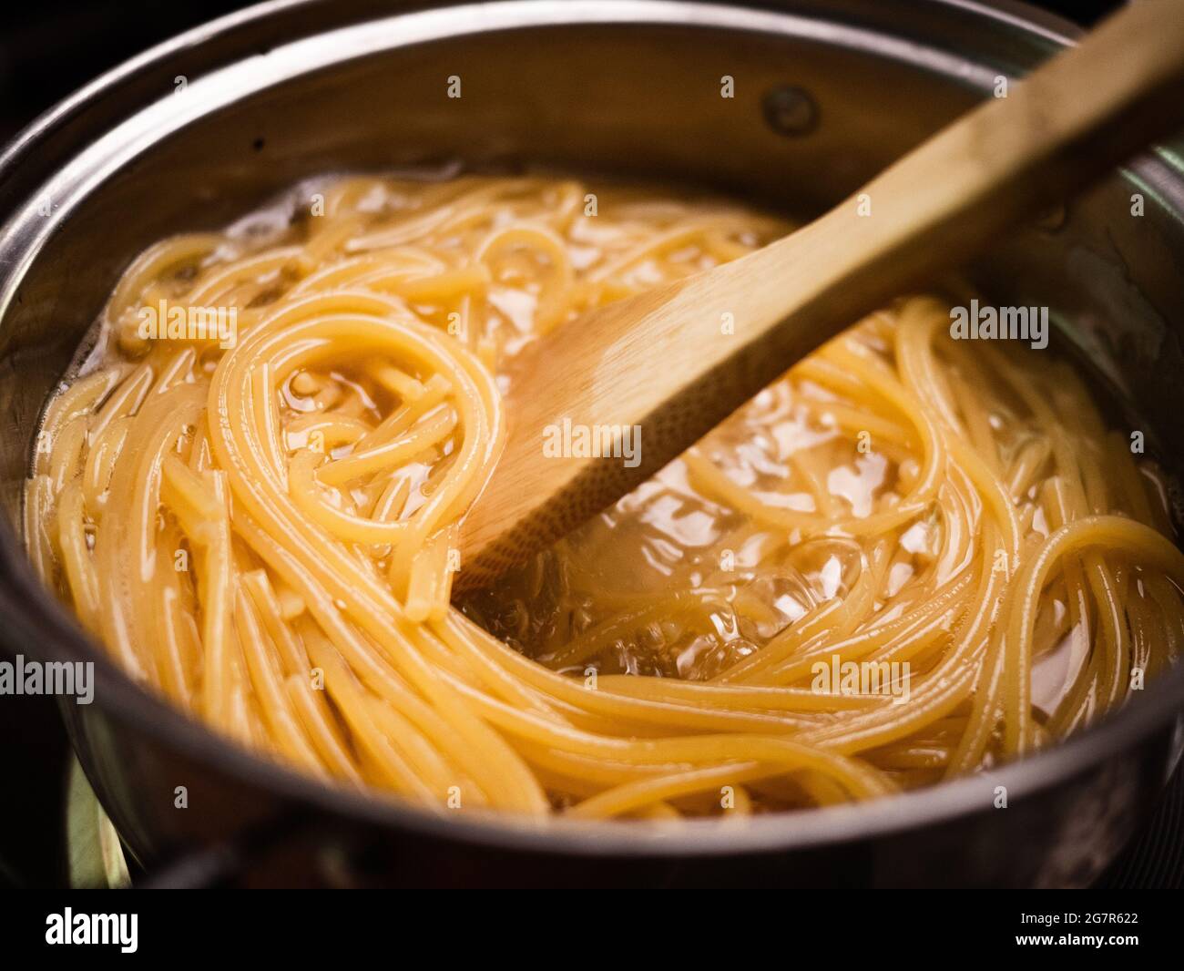Raw spaghetti is being cooked in boiling water in a kitchen pot ...