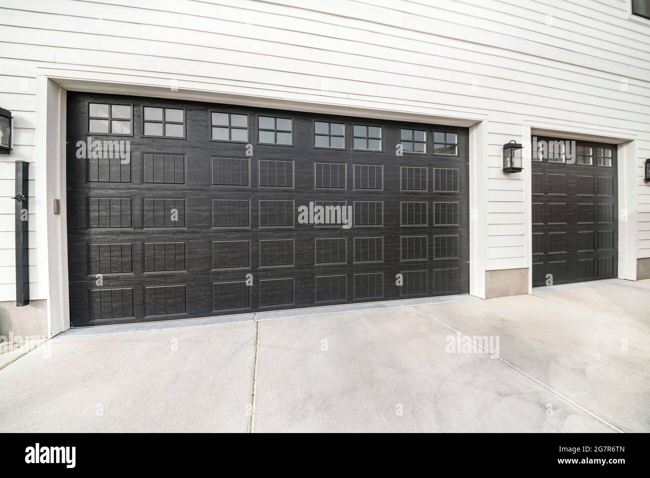 Two black garage doors with window panels and wall lighting Stock Photo ...