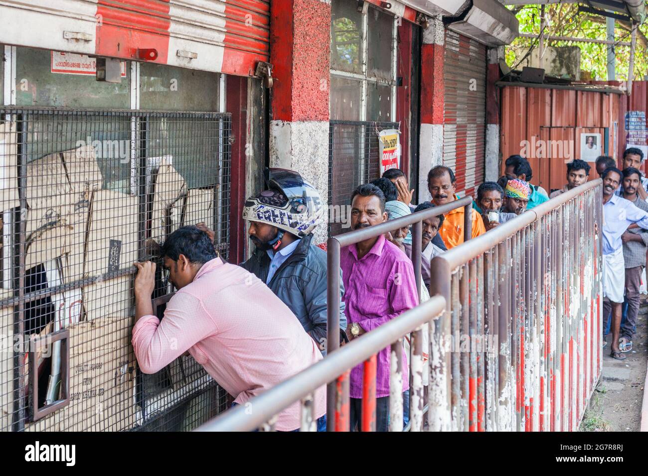 Queue of Indian men queuing at grilled window of liquor store in street ...