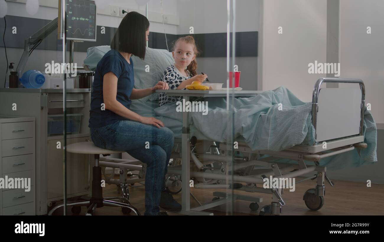 Sick child patient sitting in bed with oxygen nasal tube eating healthy ...