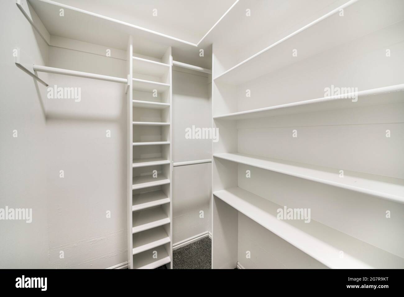 Small empty walk in closet with white interior and built in shelving ...