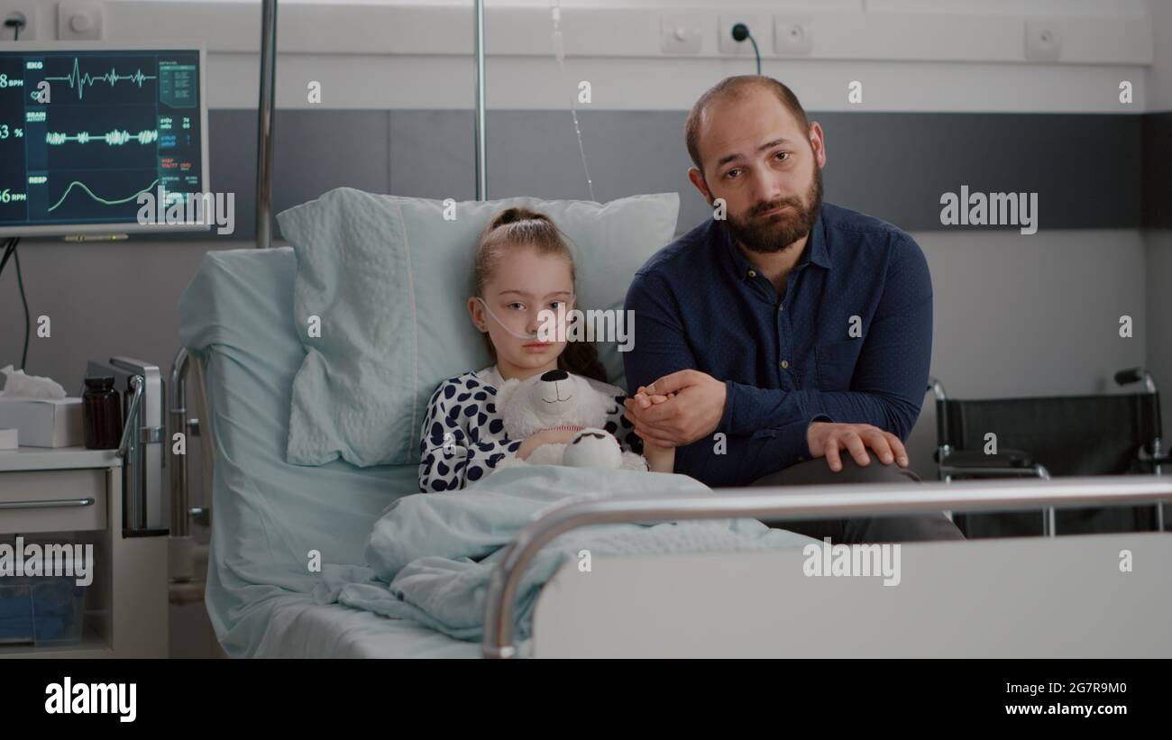 Portrait of worried father holding hospitalized sick daughter hand ...